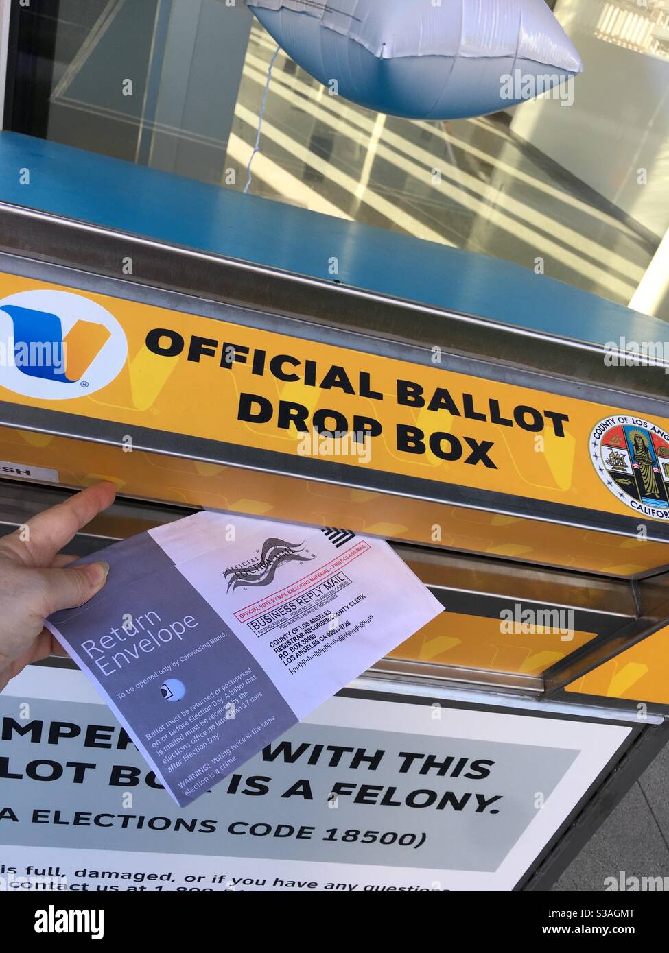 A hand dropping a mail-in ballot into an official Los Angeles County ...
