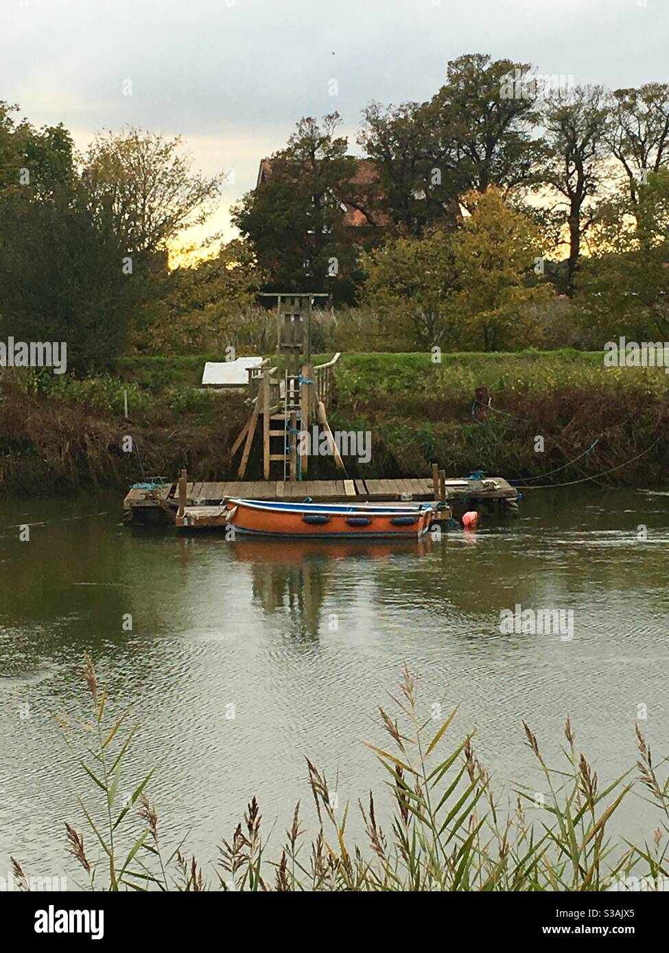 Small Orange rowing boat moored on river next to wooden jetty Stock ...