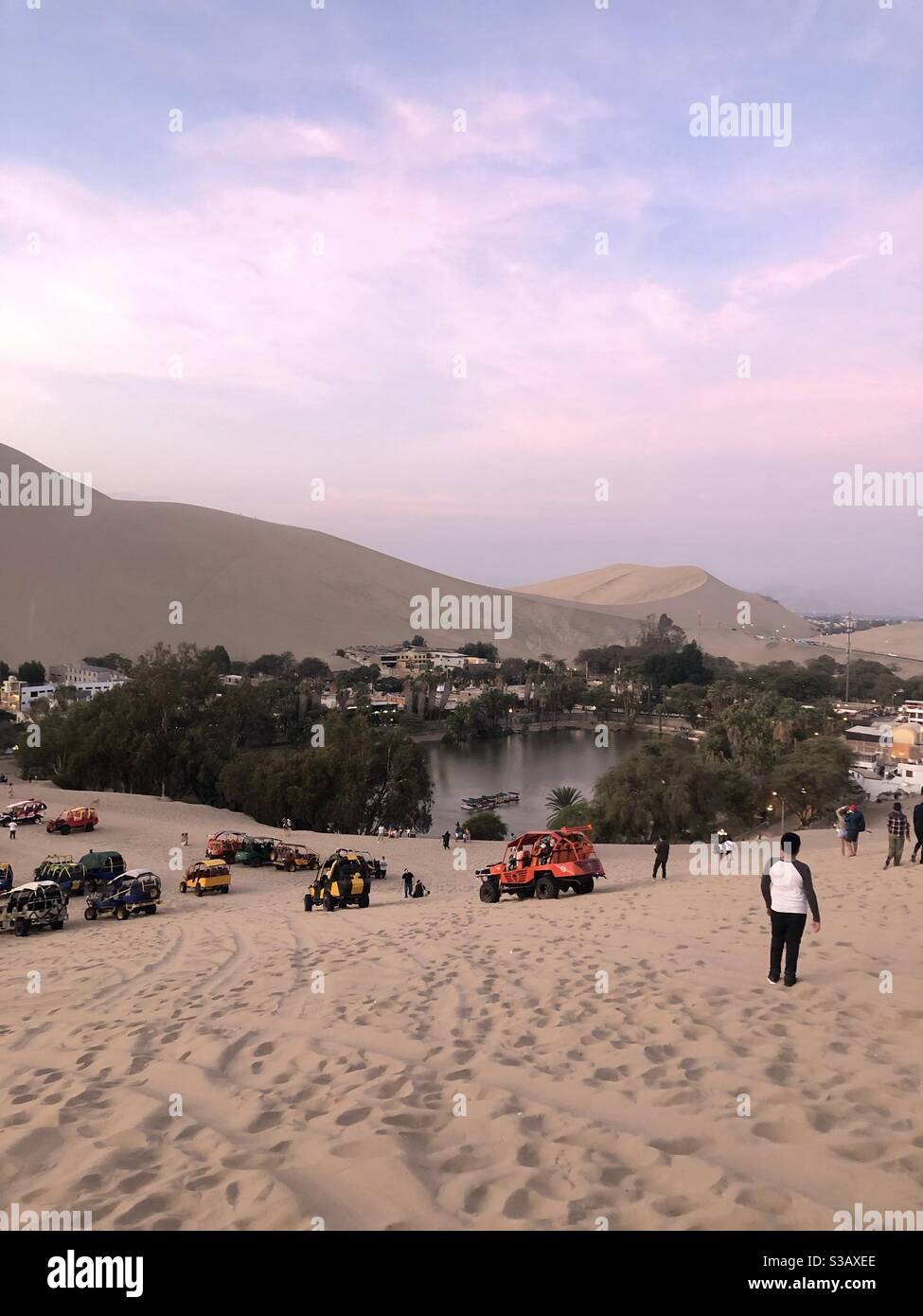 Huacachina Lagoon encircled by palm trees and sand dunes. Tourists rent ...