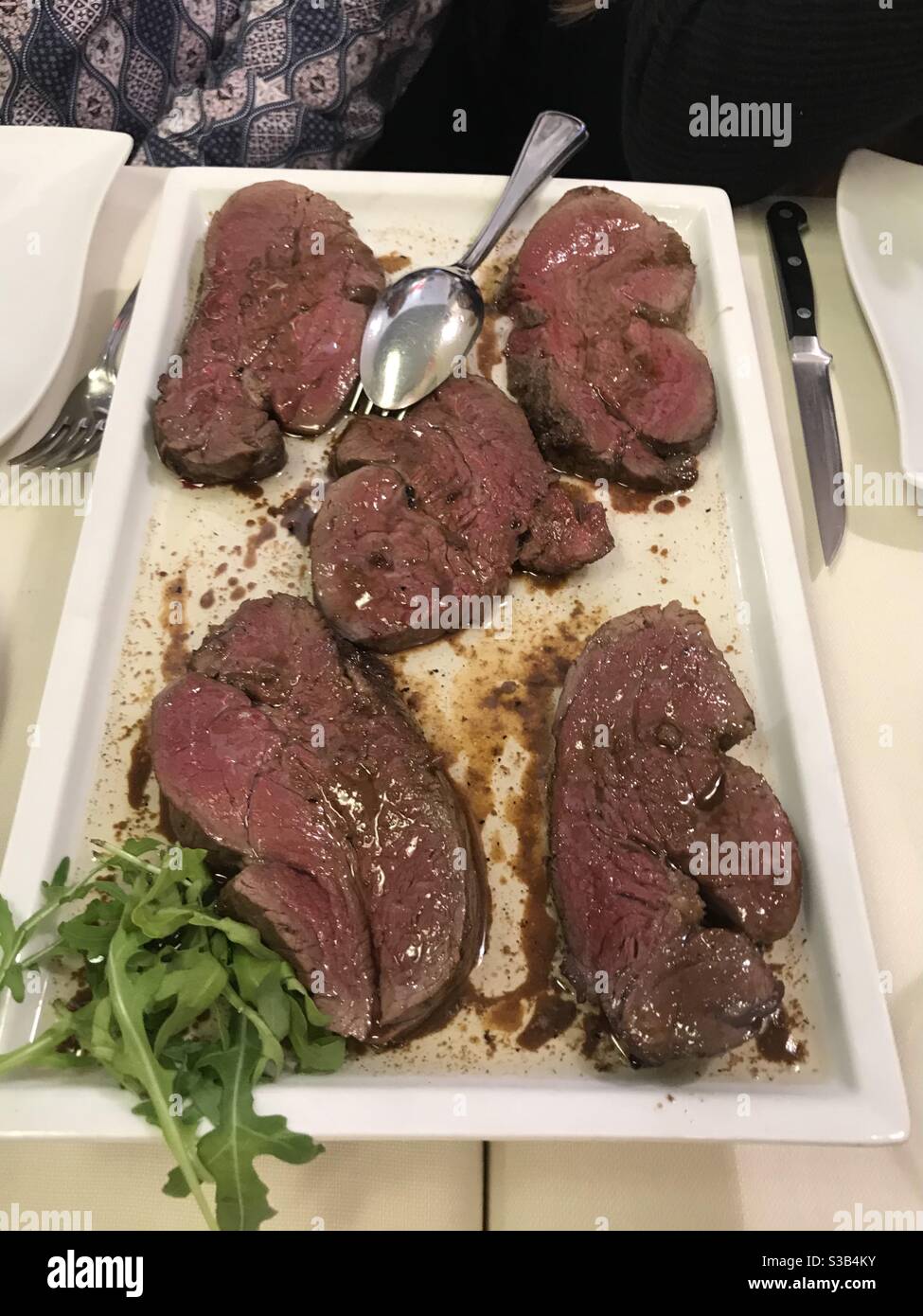 A platter of medium rare steaks garnished with rocket and served in an ...