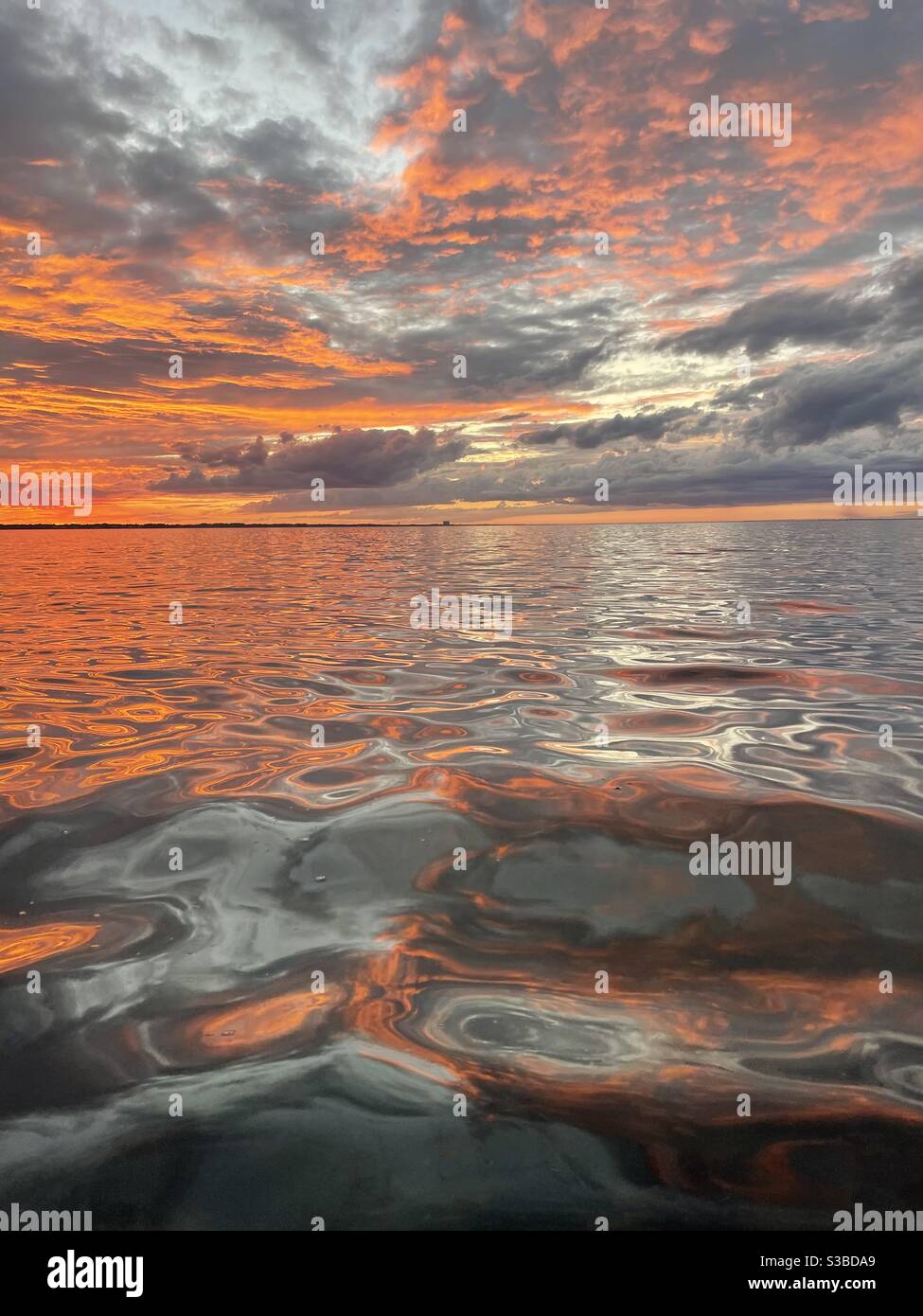 Low perspective sunset over bay water with colorful reflections and ...
