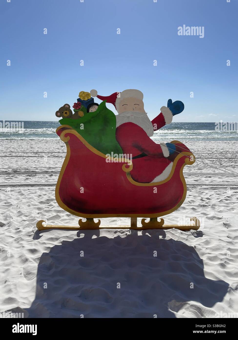 Santa in a red sleigh with gifts on white sand beach with view of ocean ...