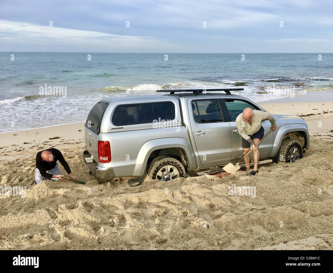 Two men digging out beach sand from under their bogged vehicle Stock ...