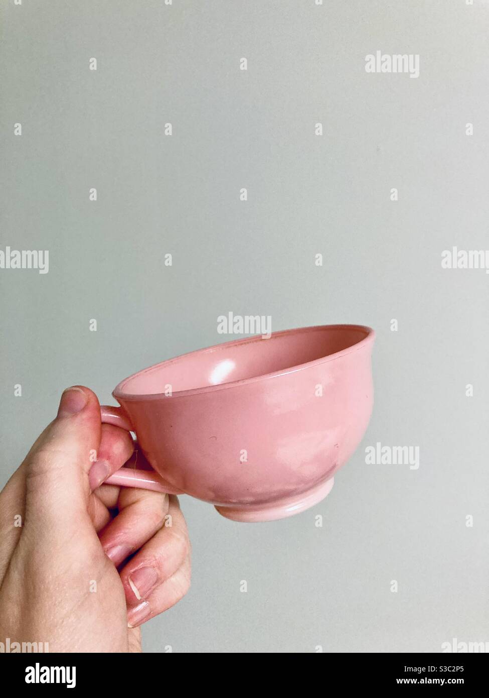 Anonymous hand raising a pink ceramic teacup against a solid taupe ...