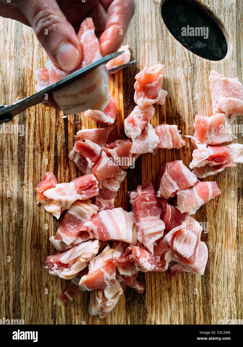Cutting streaky bacon into small pieces with a pair of scissors Stock ...