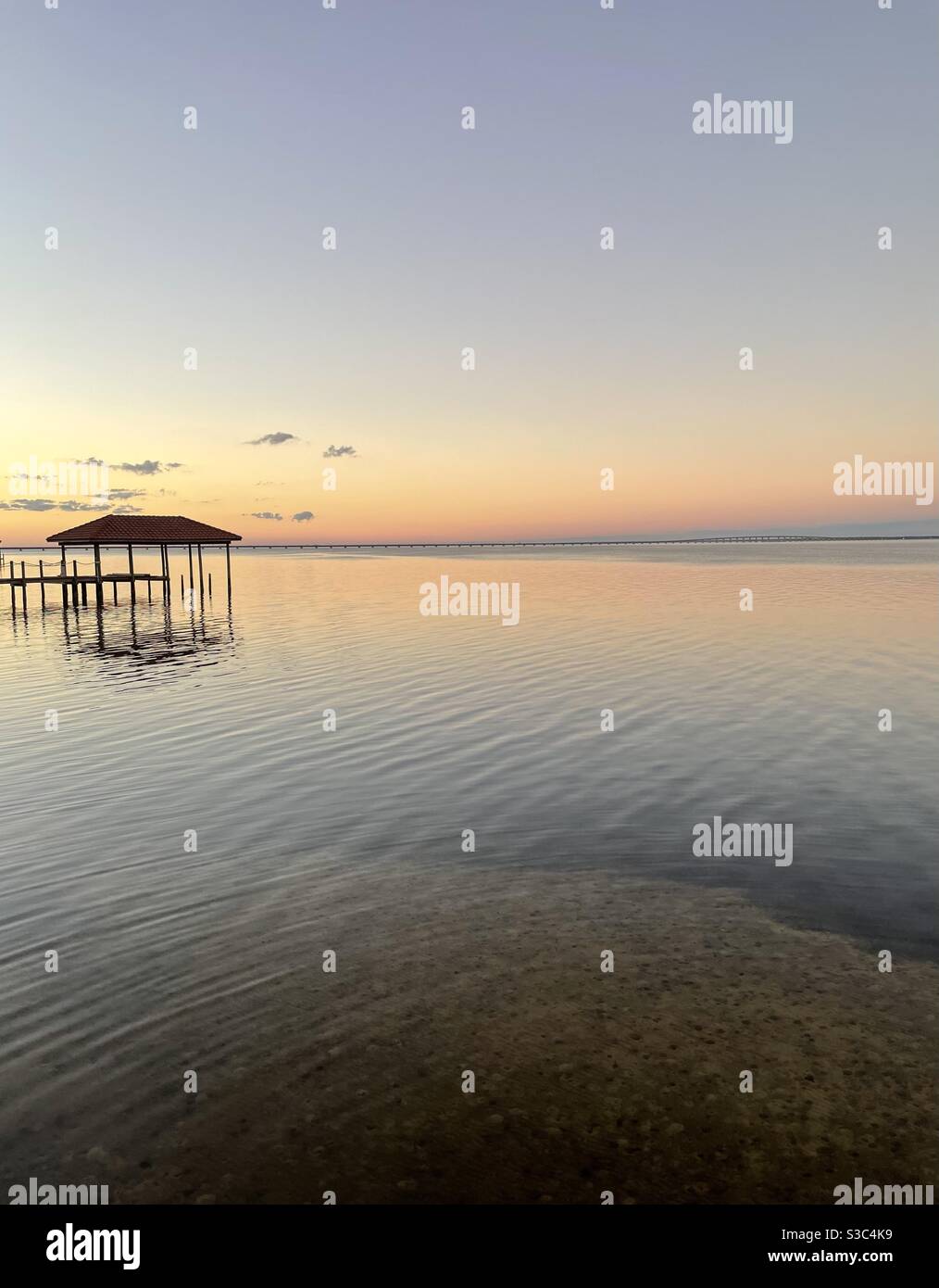 Sunset skies with boat dock at low tide over bay water Stock Photo - Alamy