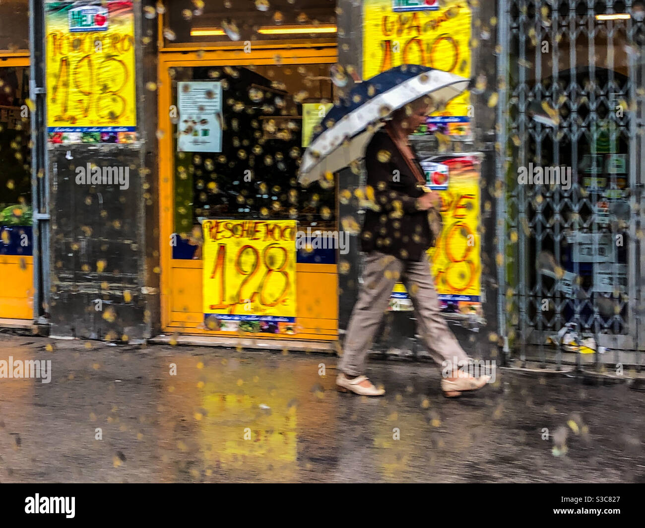 A woman with an umbrella walking past the shop windows in the rain ...