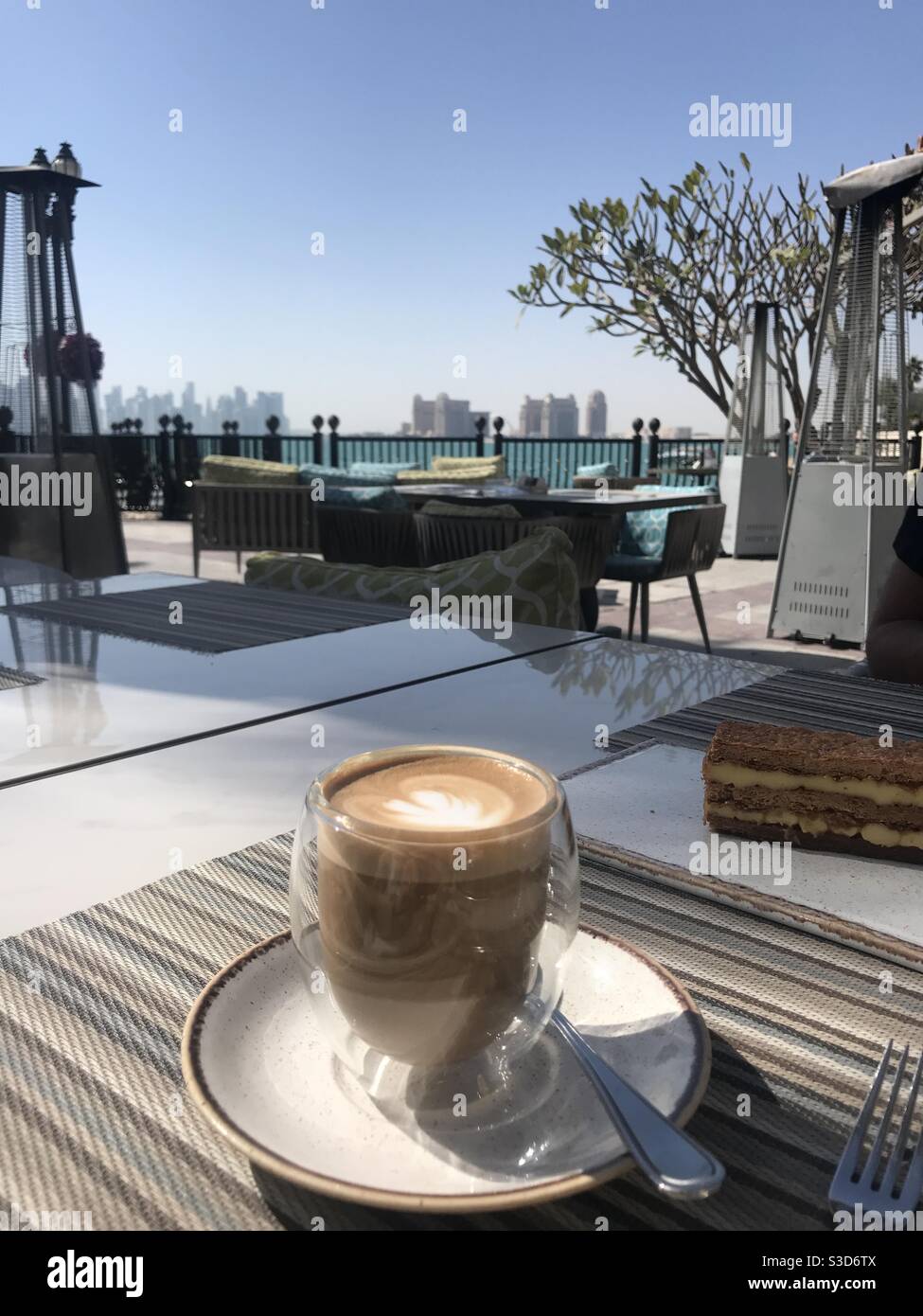 A cup of cappuccino coffee on a restaurant terrace overlooking the Doha ...