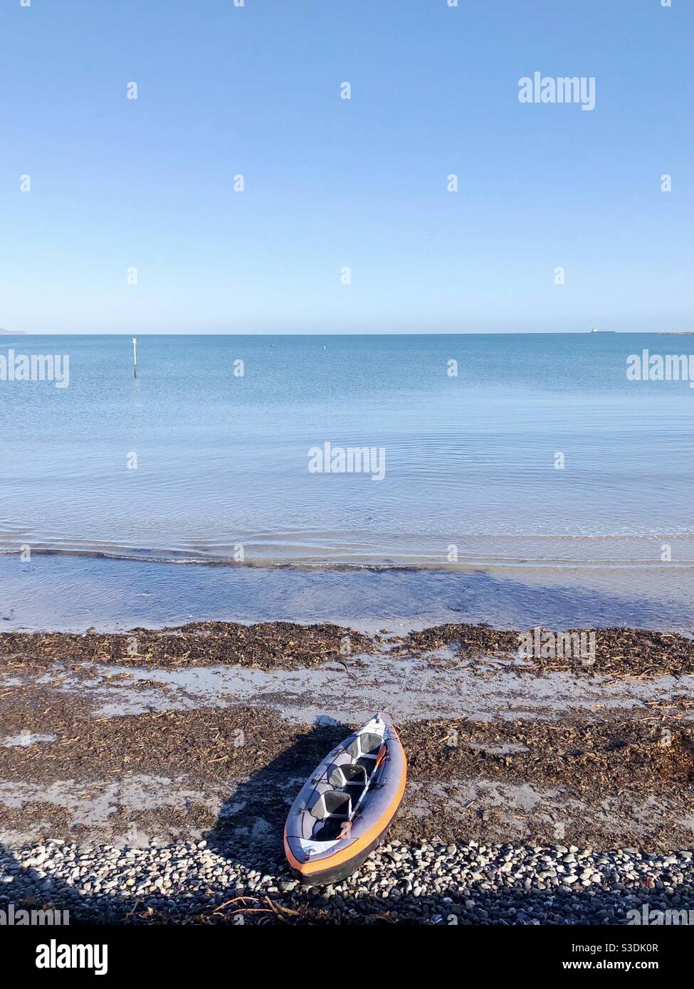Inflatable canoe on a seaweed covered beach with calm sea in background ...