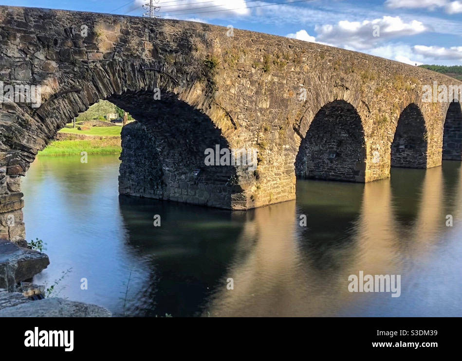 Calm water flows under a Roman stone bridge, on a pleasant summer’s day ...