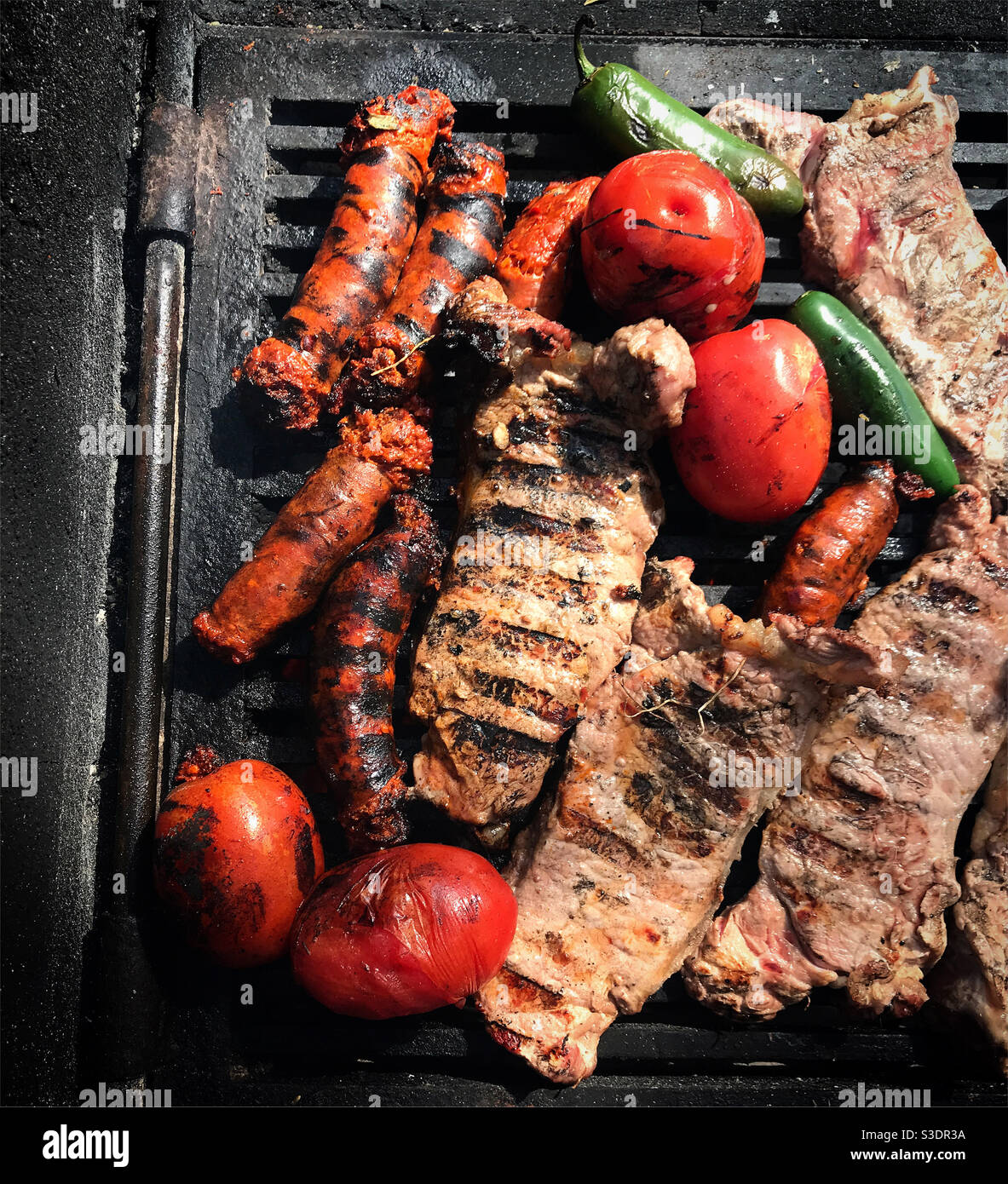 Grilled parrilla with sausage, tomatoes, green chilli peppers and meat ...