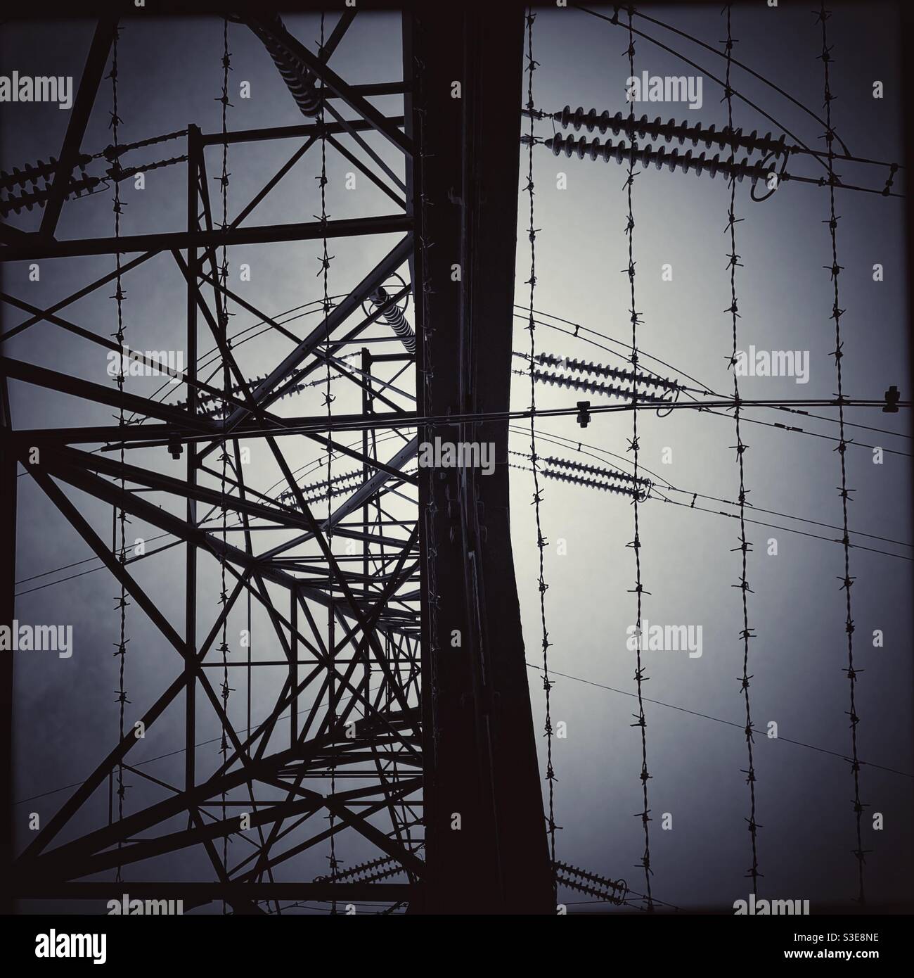 View underneath electricity pylon up towards sky showing barbed wires ...