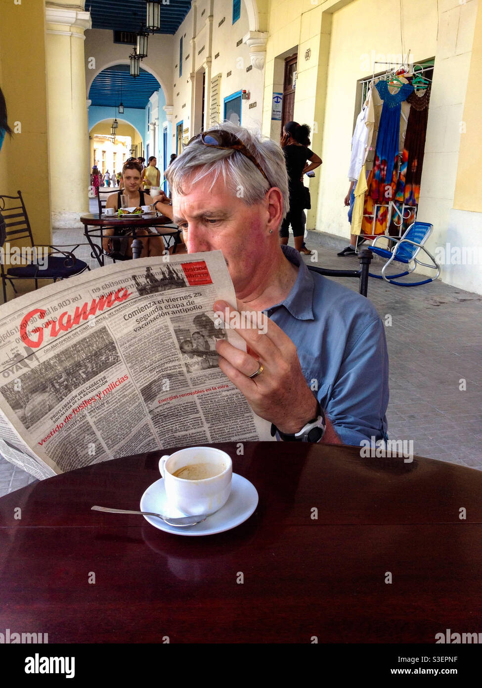 Male tourist reading local Granma newspaper at cafe table with coffee ...