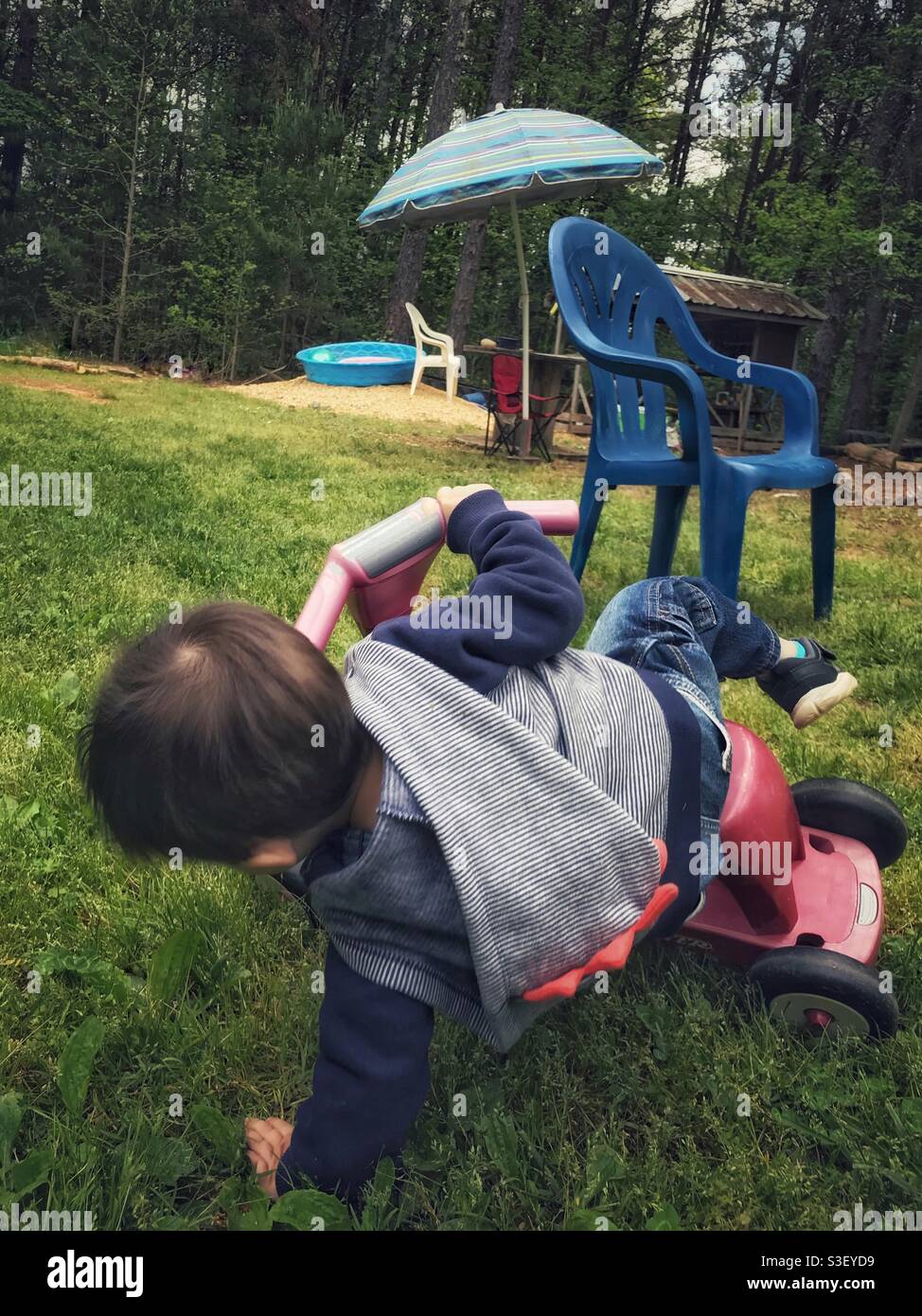 Toddler falls from red ride-on toy in yard Stock Photo - Alamy