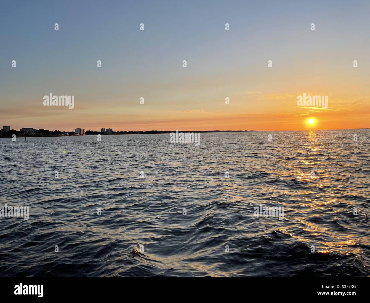 Sun setting low on the horizon over bay water Stock Photo - Alamy