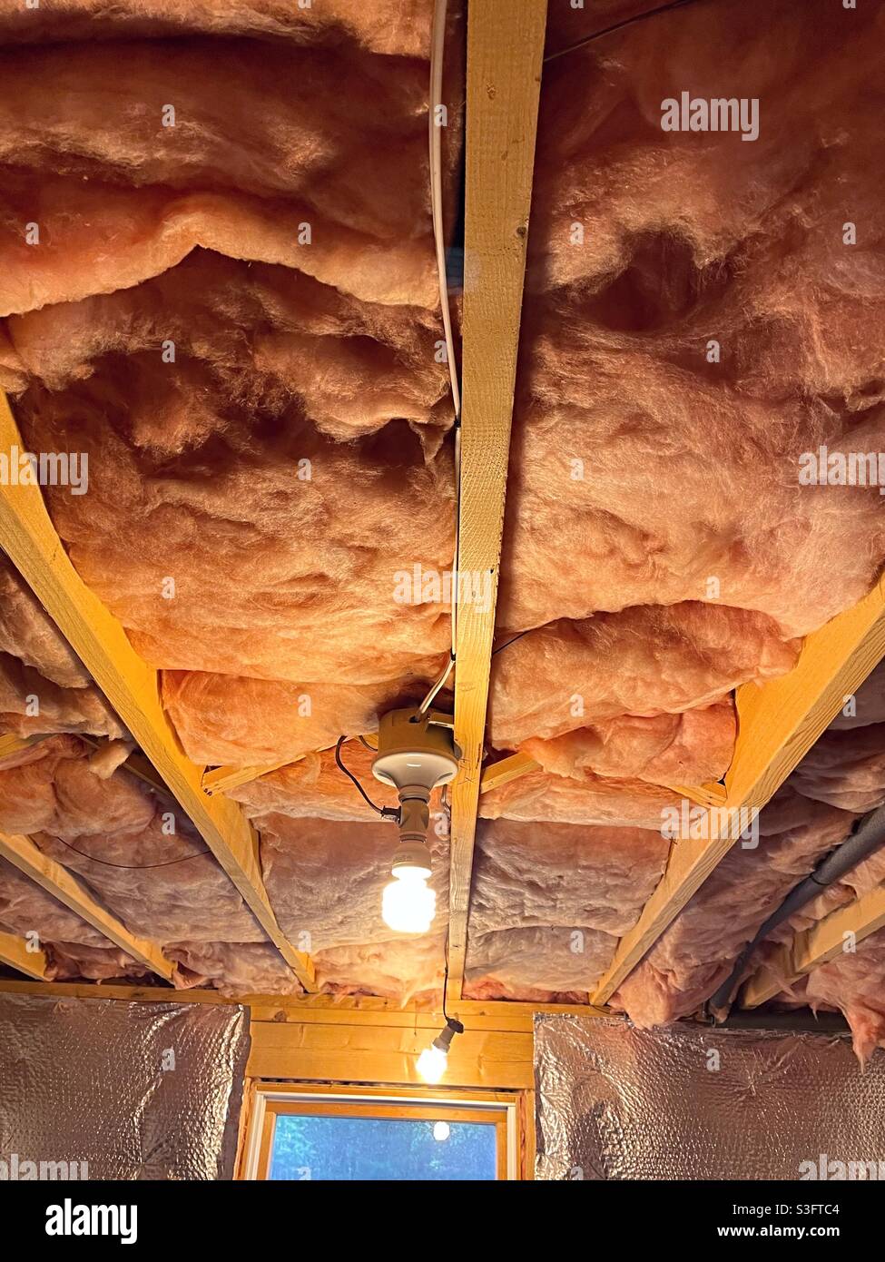 Home fiberglass insulation in an unfinished ceiling with a lightbulb ...