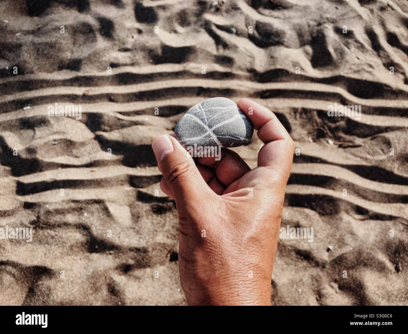 Hand holding a rock over sandy beach Stock Photo - Alamy