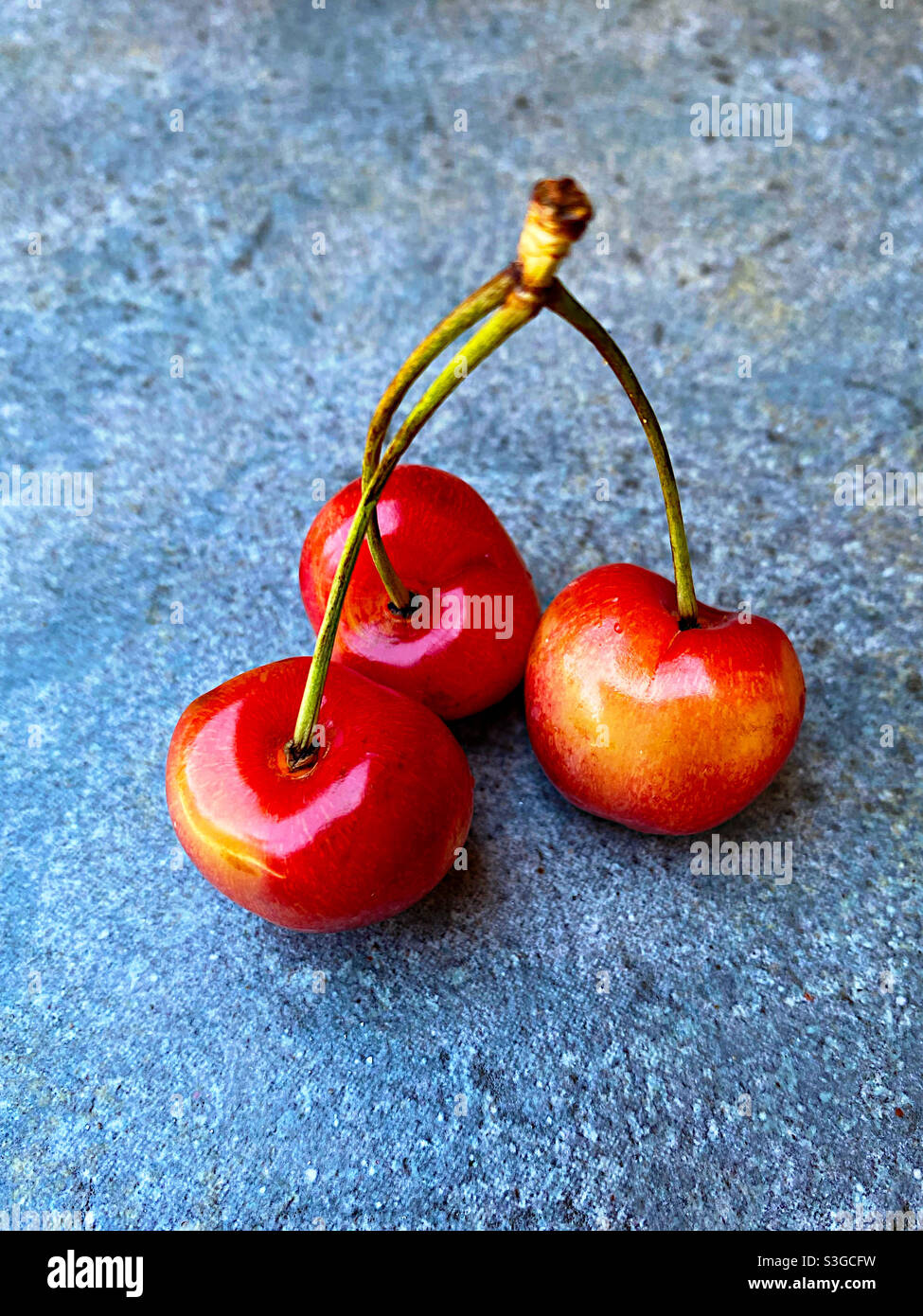 Three fresh cherries with stems on a stone surface Stock Photo - Alamy