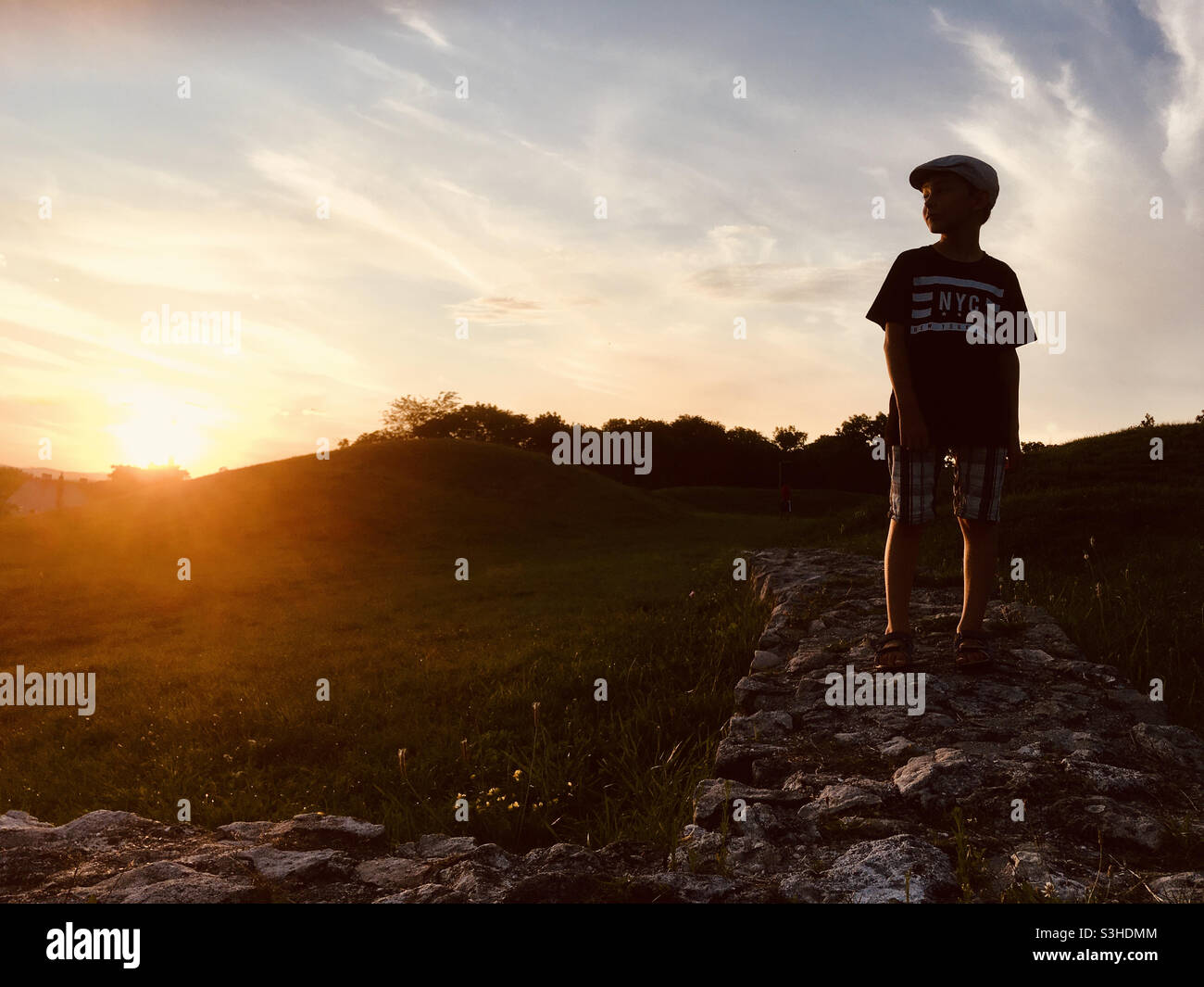 Boy child standing on Ancient Roman stone wall remains with setting sun ...