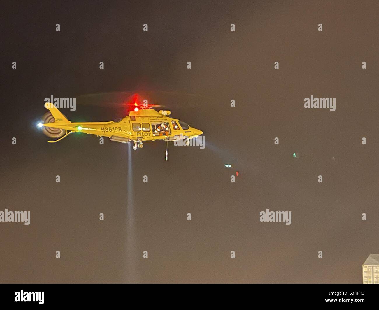 Yellow helicopter in the night approaching merchant container vessel to ...