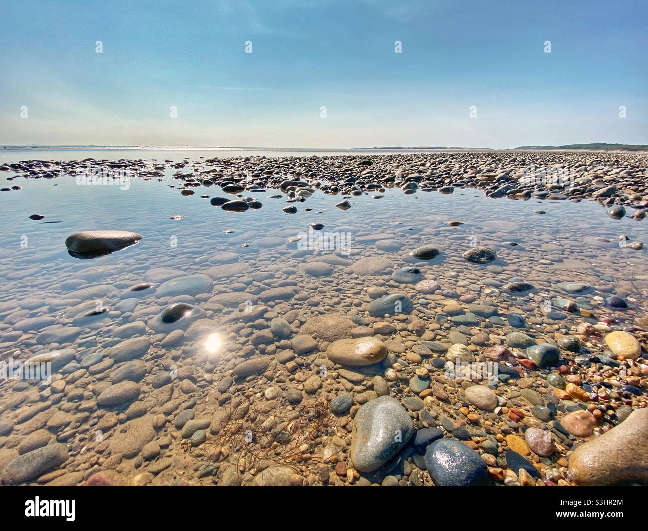 Sunshine glistening on pebbles and water on a shingle beach, Newborough ...