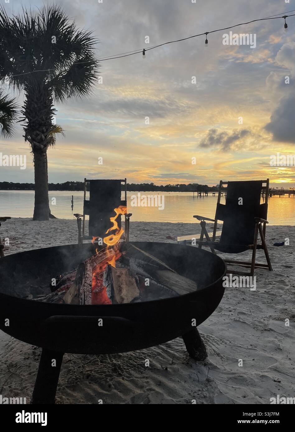 Outdoor fire pit on white sand with chairs, palm tree and sunset skies ...