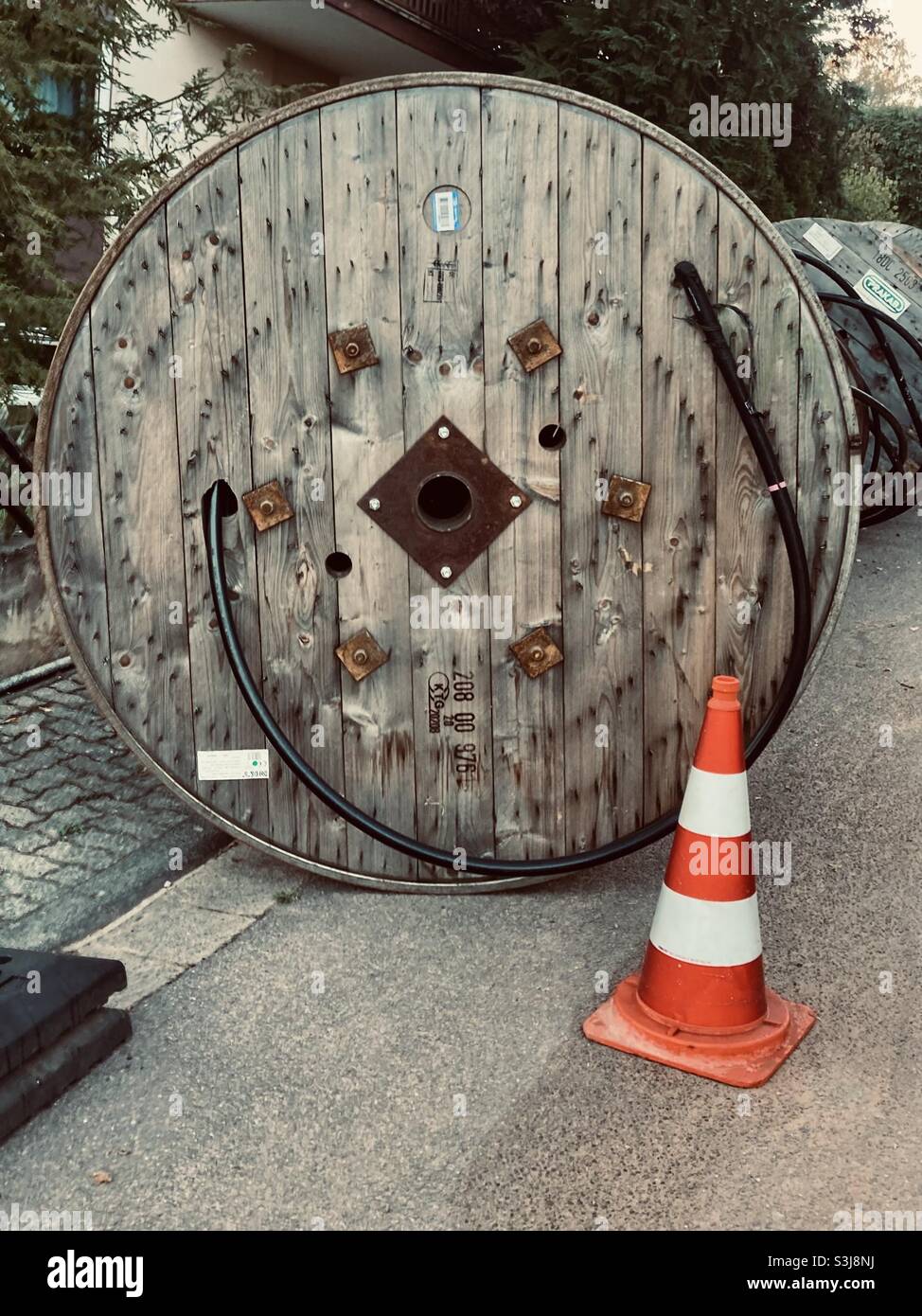 A cable drum cordoned off with a pylon stands at a roadside ...