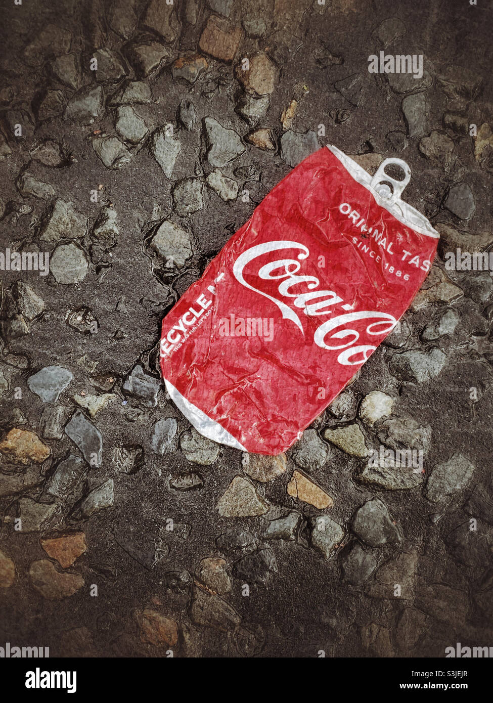A squashed can of Original Taste Coca-Cola lies on the side of a road ...