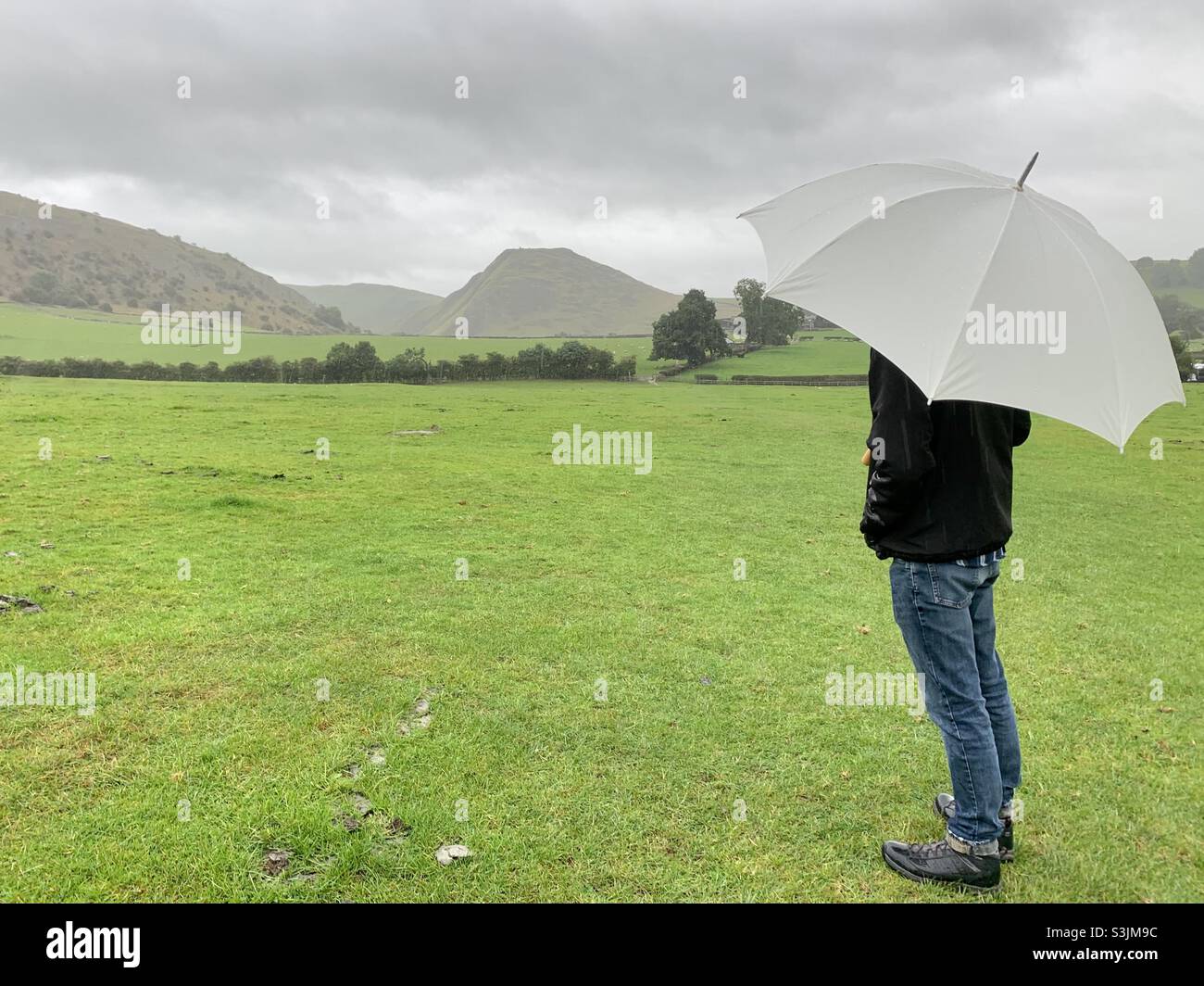 Man with cream umbrella in rainy field in the Peak District Derbyshire ...