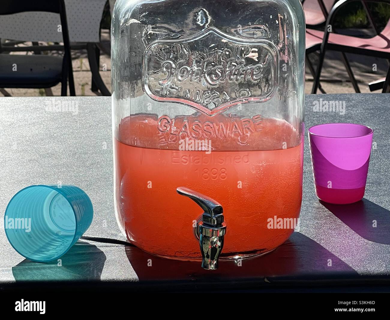 A glass drink dispenser is filled with pink lemonade for a summer ...