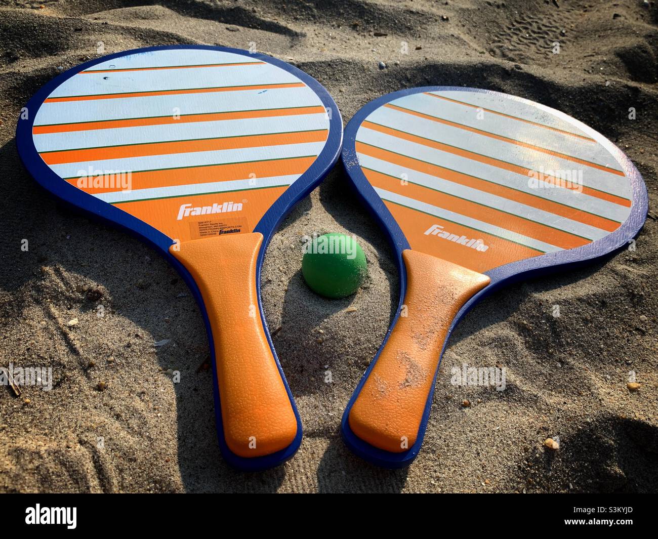 Orange, white and blue Kadima paddle board. Lying down on the sand ...