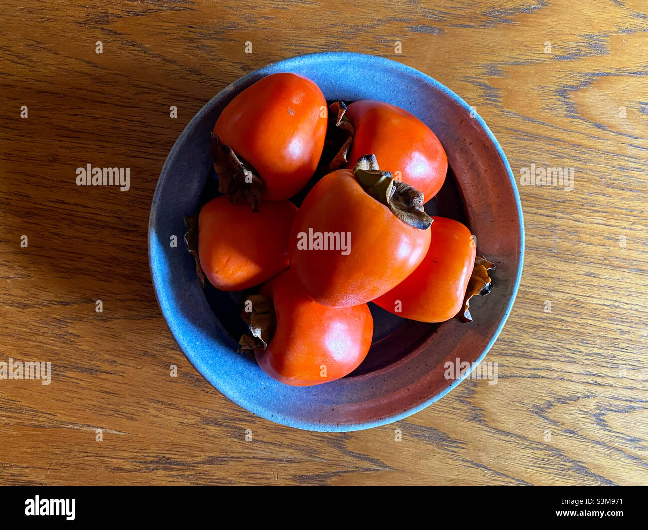 Blue bowl with rip persimmons Stock Photo - Alamy