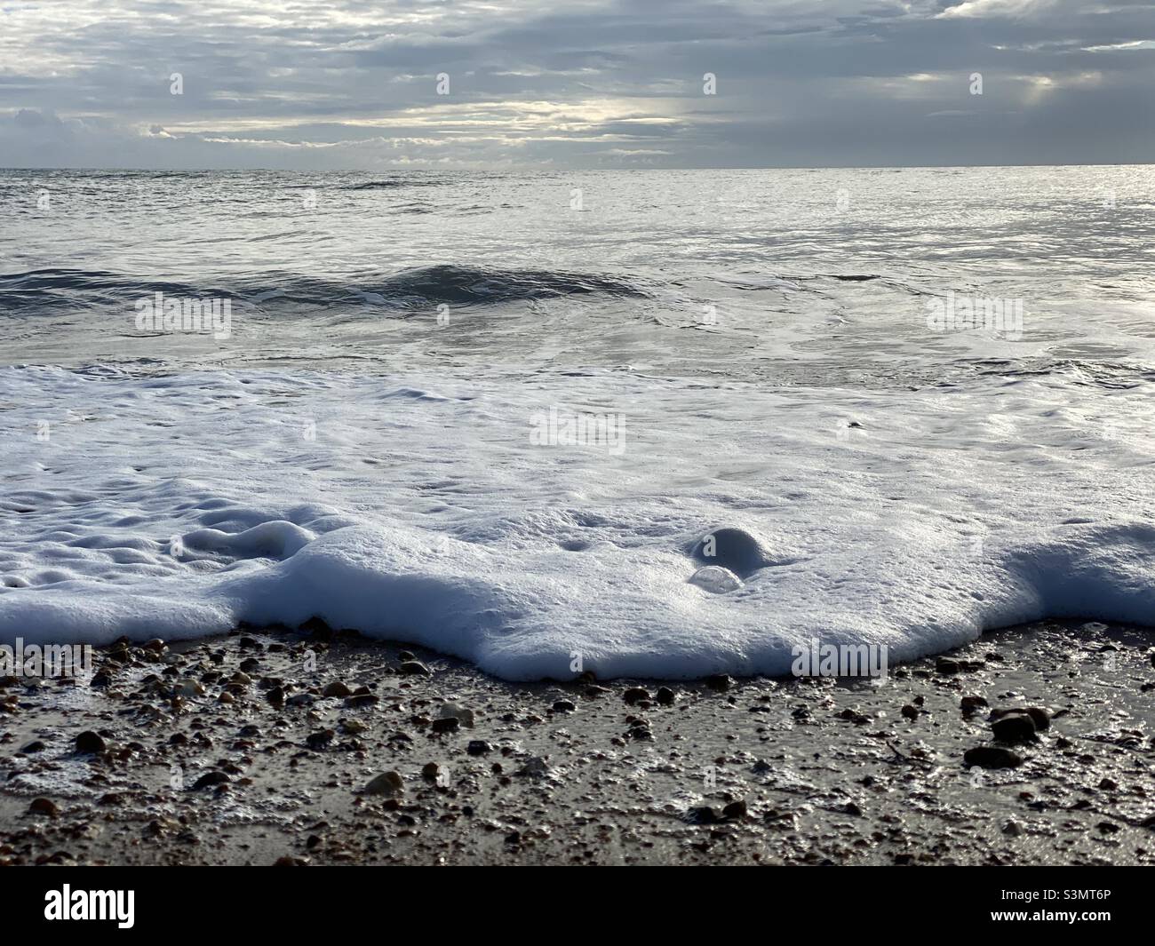 Frothy wave creeping up beach Stock Photo - Alamy