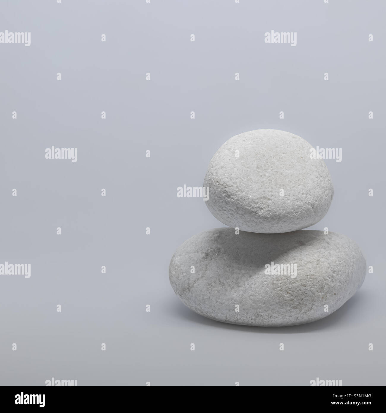 Two white pebbles, one balanced on the other against a pale grey ...