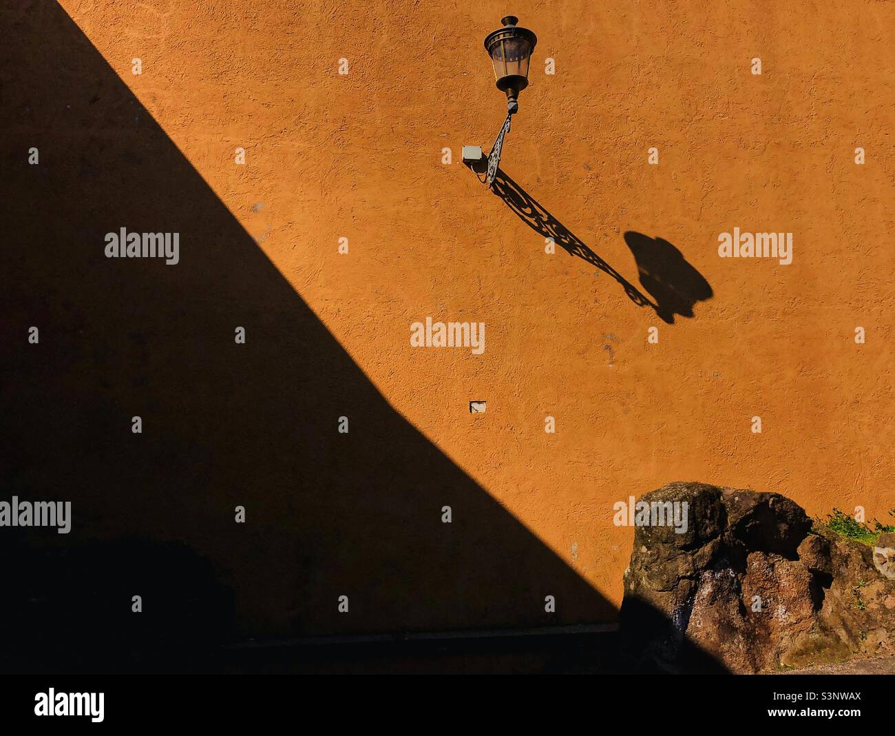 Lamp post and shadow on an orange color wall in Italy Stock Photo - Alamy