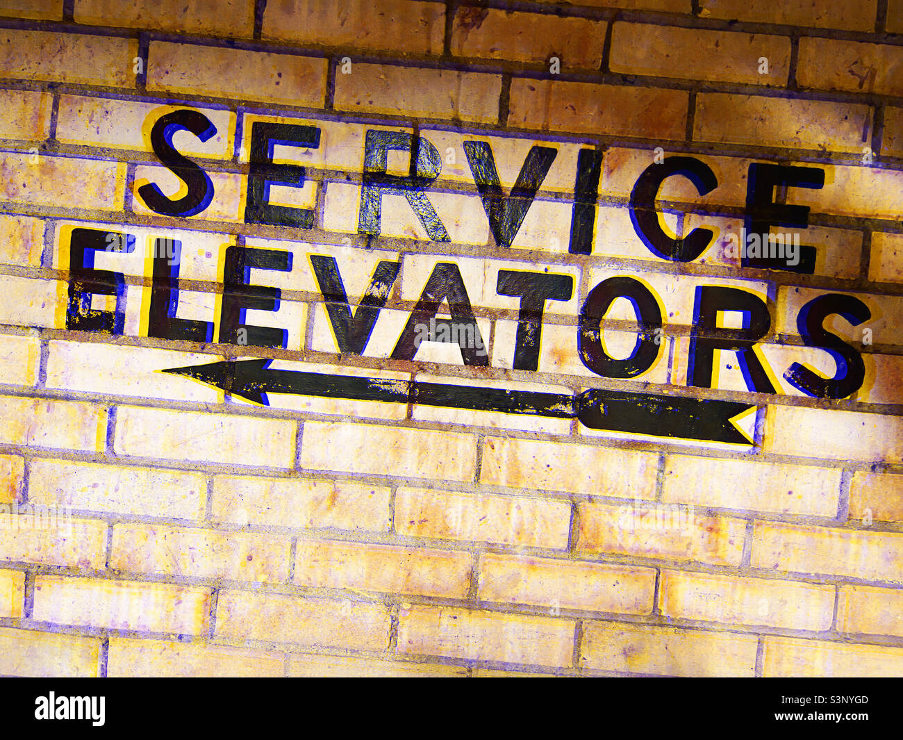Service elevator sign with directional arrow on a brick wall in urban ...