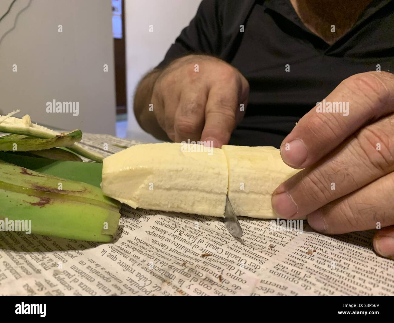 Human hand cutting a plantain in halves to prepare ‘tostones’ using a ...