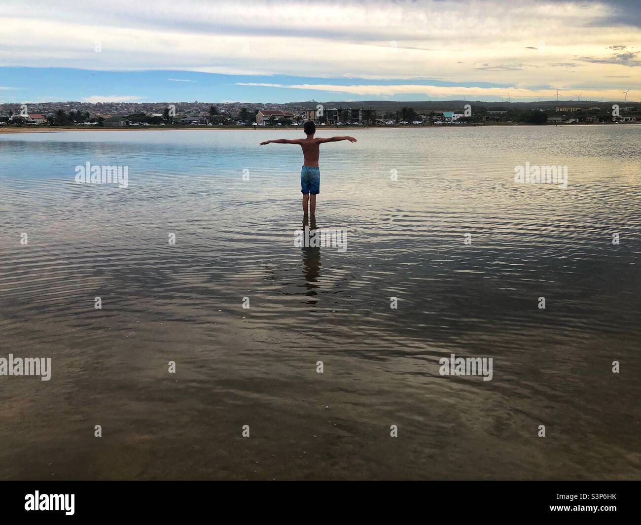Think young boy standing in a calm lagoon with his arms outstretched ...