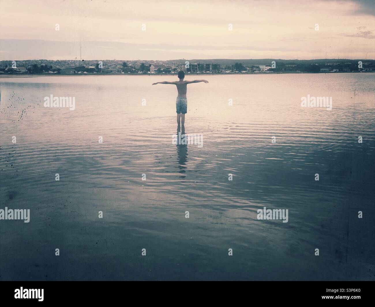 Young boy standing with his arms outstretched in a shallow body of ...