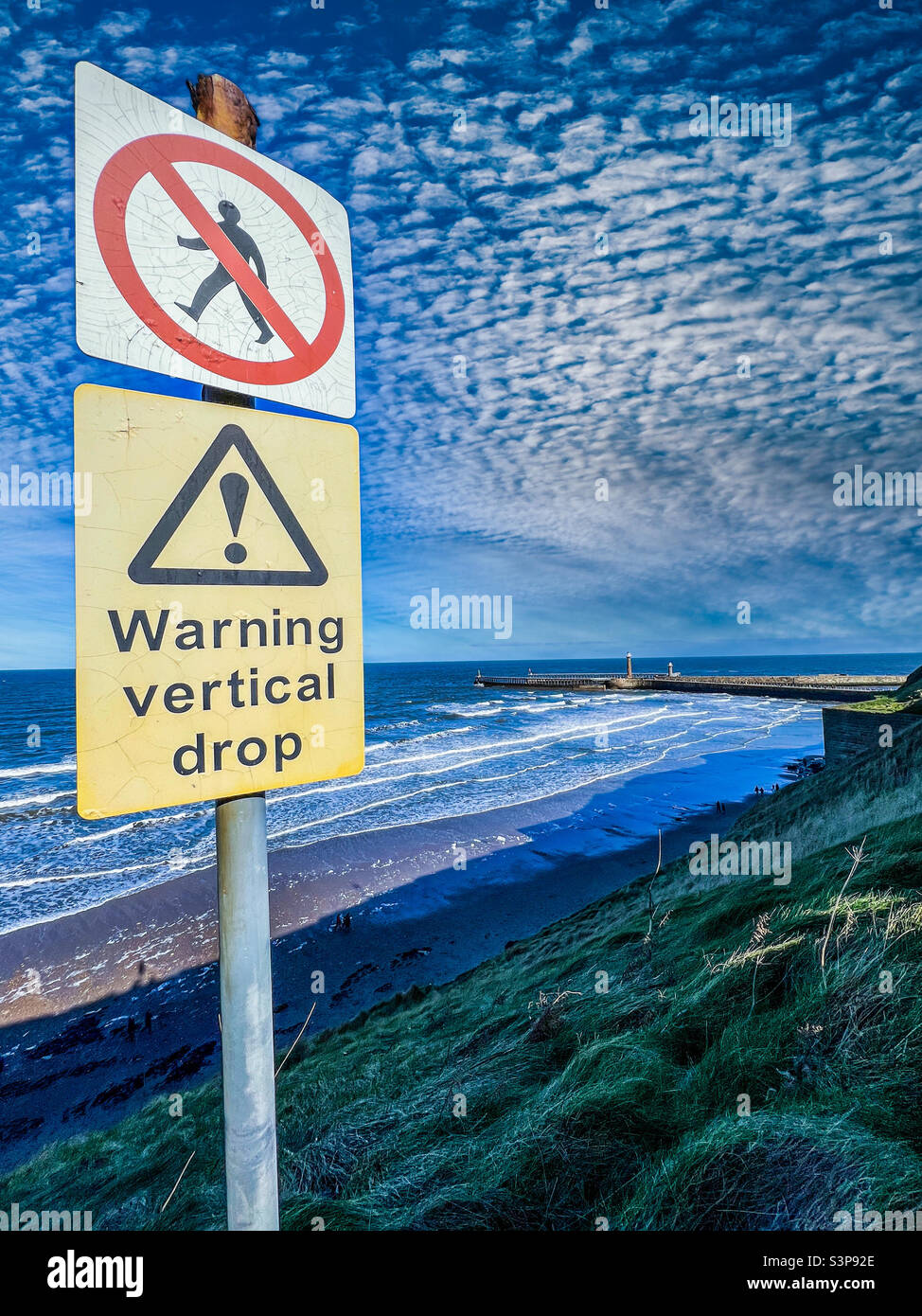 Vertical drop warning sign overlooking Whitby beach and harbour in ...