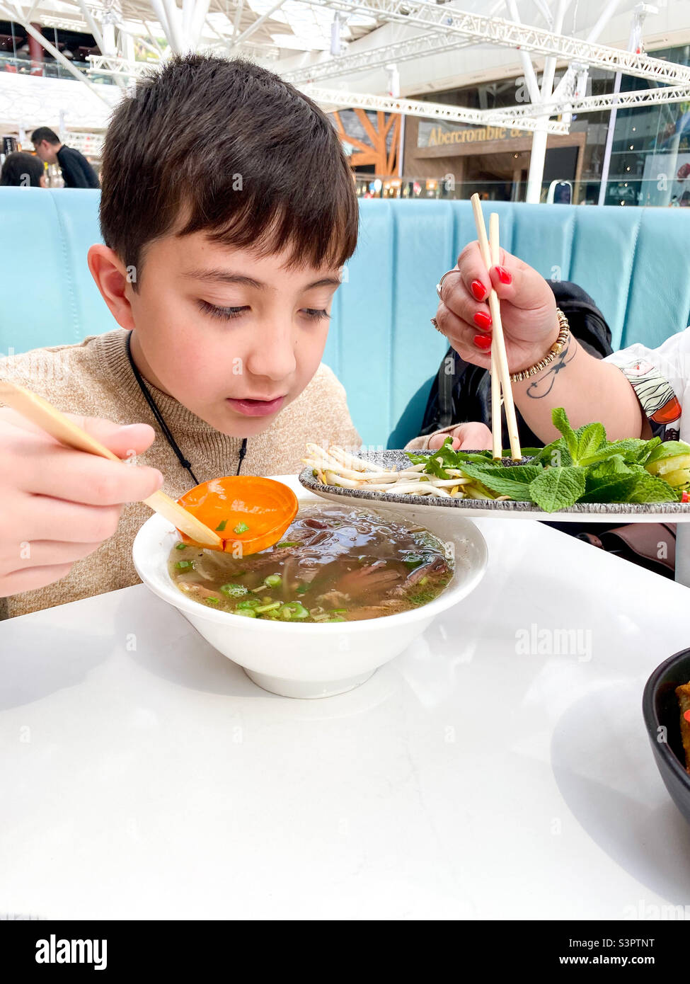 A boy eating a bowl of Vietnamese pho in a food court Stock Photo - Alamy