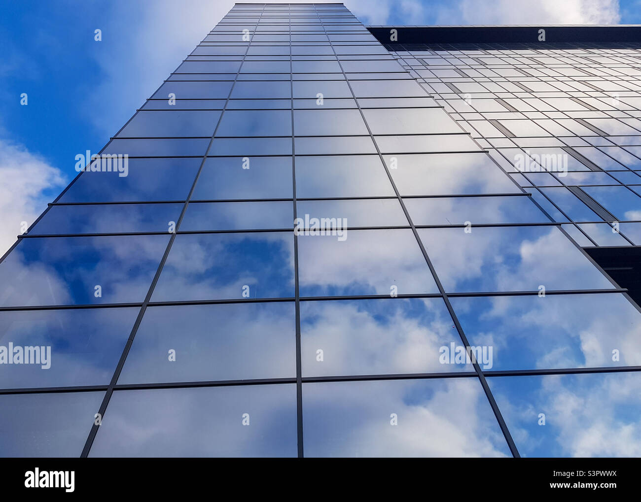 View of a modern glass skyscraper. Reflection of a cloudy blue sky in a ...