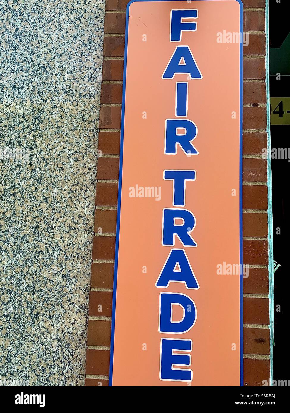 Orange and Blue, FAIR TRADE Sign and Red Brick Wall Stock Photo - Alamy