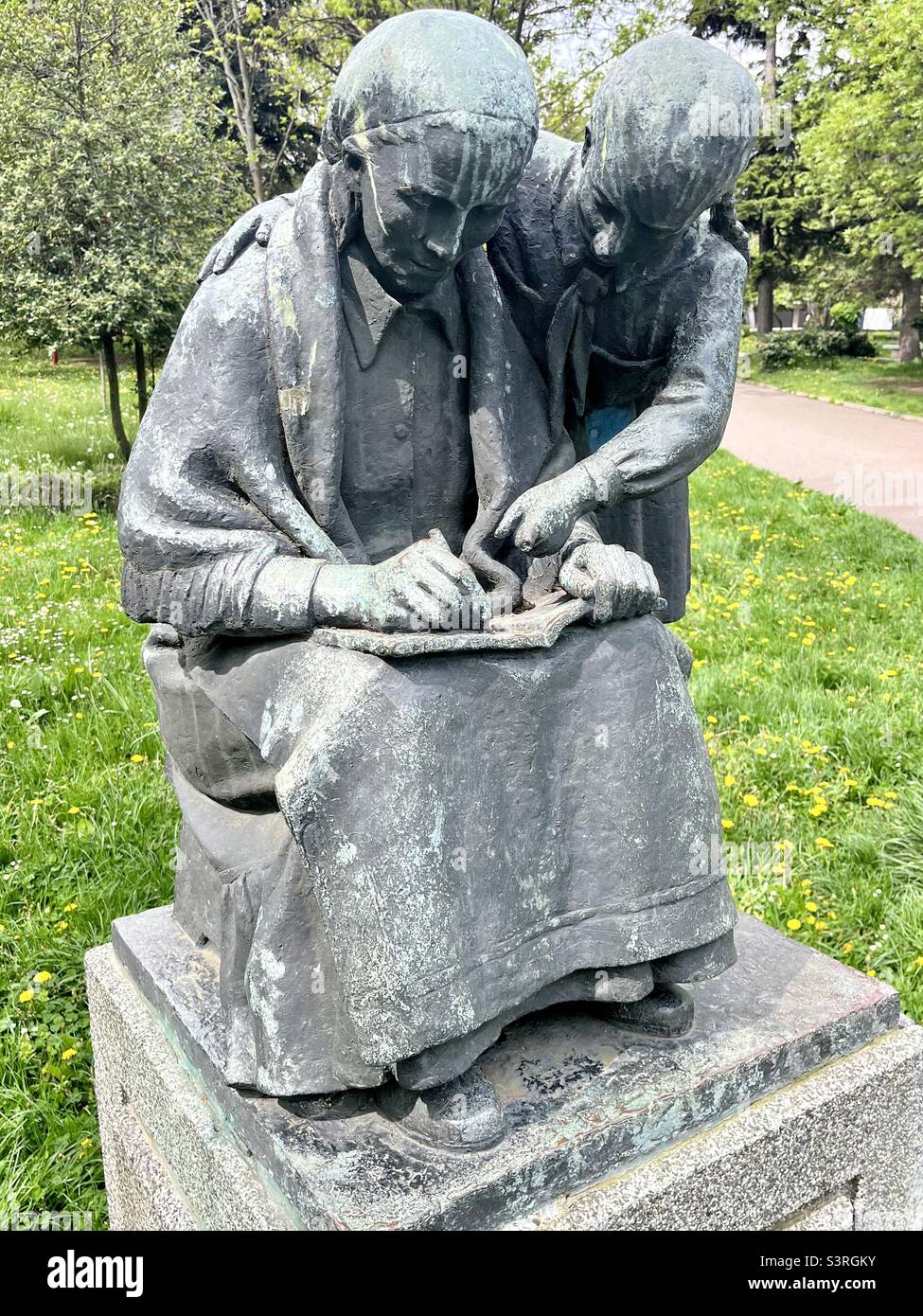 Garden statue depicting grandmother and granddaughter reading a book in ...