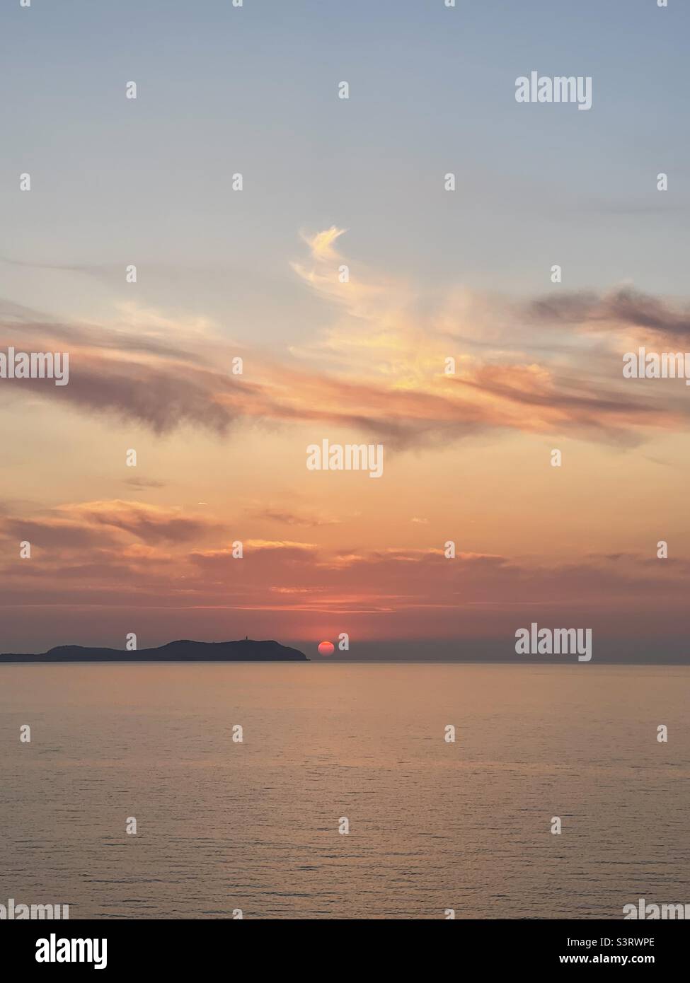 Cloudy red sunset over an island Stock Photo - Alamy