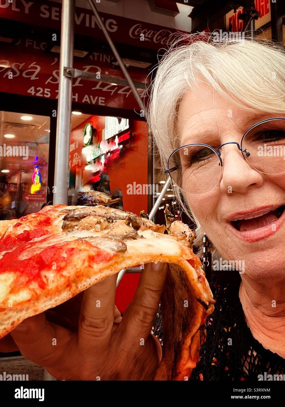 Woman taking a bite of a large slice of pizza Stock Photo - Alamy