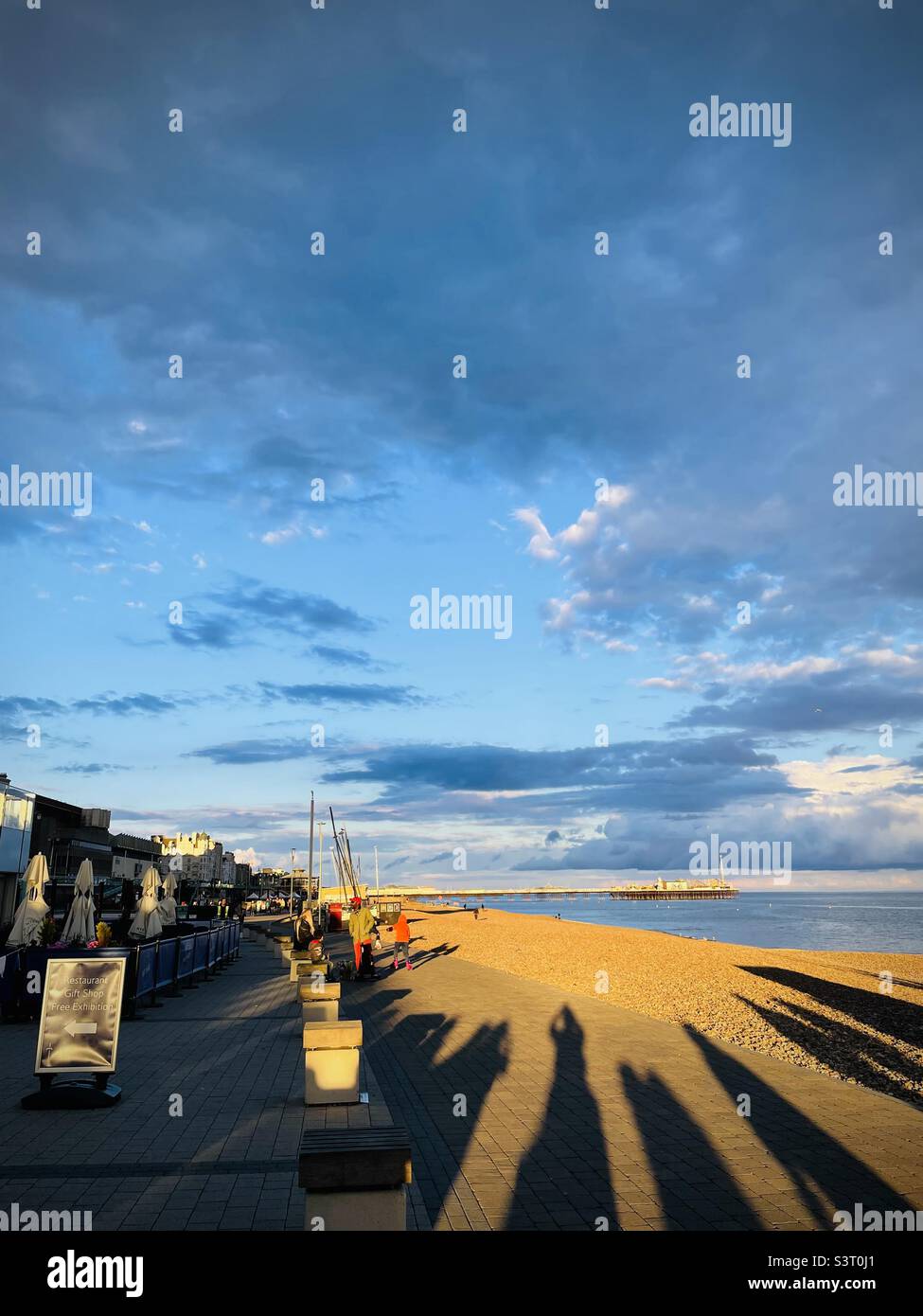 Brighton seafront at sunset with people’s shadows in the foreground ...