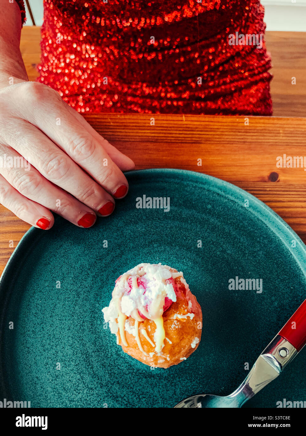 Plate with a single profiteroles next to a woman wearing a red sequin ...