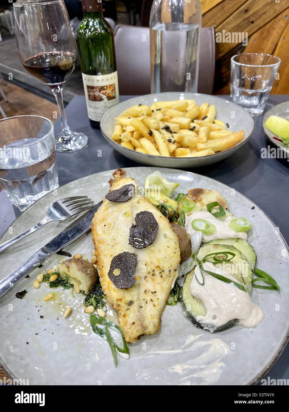 Grilled fillet of fish topped with sliced truffles and a bowl of potato ...