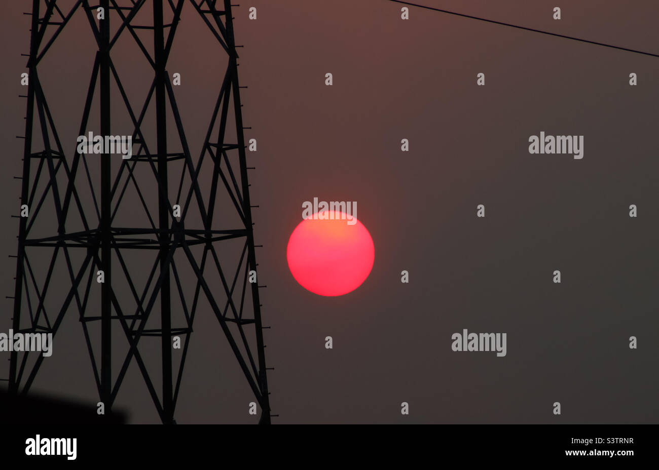 Ball of red sun, sets beside a pylon Stock Photo - Alamy